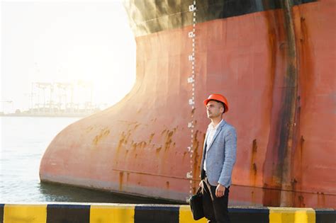 회색 양복과 보호 건설 오렌지 헬멧 경우 녹슨 화물선 물 선 배경에 대 한 항구에 서 있는 잘생긴 젊은 이루어지지 성공적인 비즈니스 남자 사람들에 대한 스톡 사진 및 기타