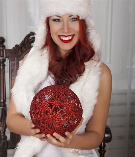 Усмехаясь девушка держит красный шарик рождества Красивая модель женщины в белом мехе Стоковое