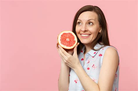 여름 옷에 예쁜 어린 소녀 분홍색 파스텔 벽 배경에 고립 된 신선한 잘 익은 자 몽의 절반 손을 잡고 찾고 사람들은 생생한