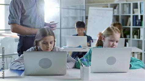 Young Male Teacher Standing And Monitoring Students Progress While