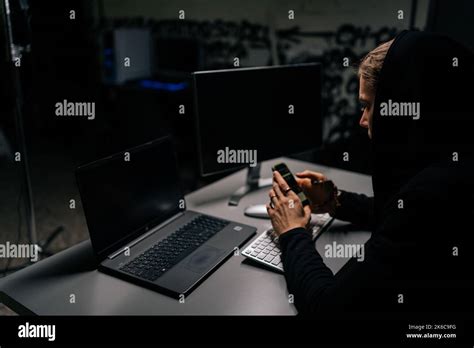 View From Back To Hidden Hacker Man Wearing Sweatshirt With Hood Engaged In Hacking Into