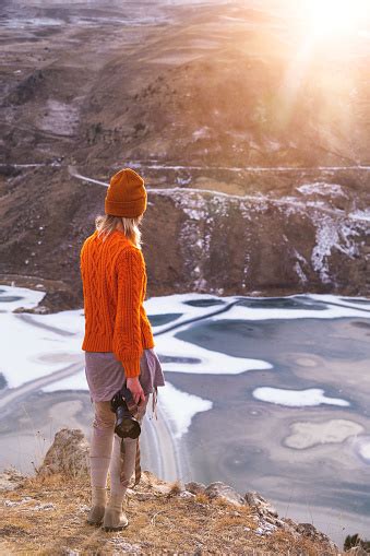 얼어붙은 산악 호수를 배경으로 산에서 카메라를 들고 오렌지 색 스웨터와 모자를 쓴 소녀 여행자 사진작가의 초상화 강에 대한 스톡 사진 및 기타 이미지 Istock