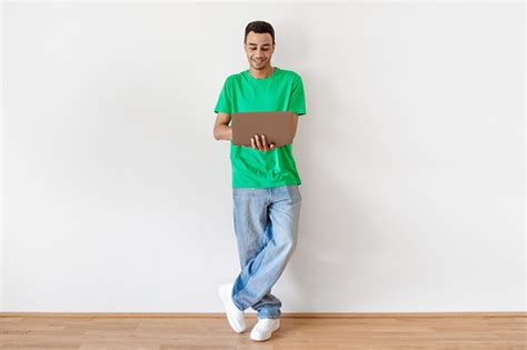 온라인 교육 프로그램 밝은 벽 위에 서 있는 손에 노트북을 들고 행복한 아랍 프리랜서 남자 전체 길이 샷 노트북 사용하기에 대한 스톡 사진 및 기타 이미지 Istock