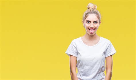 젊은 아름 다운 금발 여자는 흰색 T 셔츠를 입고 고립 된 배경 위에 혀가 재미 있는 표정으로 행복을 고집 감정 개념입니다 T