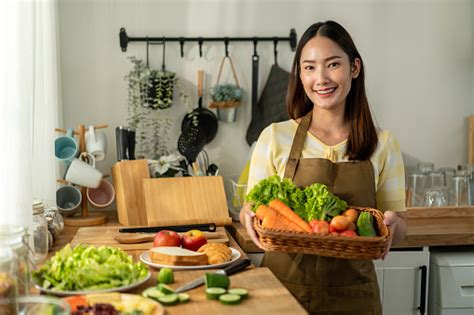 집에서 아침에 부엌에서 건강한 음식을 요리하는 여자의 초상화 매력적인 여성 주부는 재료를 준비하고 아침 식사로 그린 샐러드를 만들면서 카메라를 보면서 행복하고 편안합니다