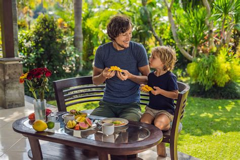 잘 생긴 젊은 남자 가 일부 커피를 붓고 그의 귀여운 아들 아침 식사 시간에 맛 있는 과일을 먹고 멋지게 제공 하는 두 먹는 가족 2명에 대한 스톡 사진 및 기타 이미지