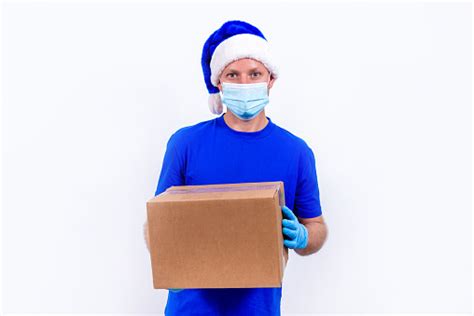 จัดส่งในเครื่องแบบสีฟ้า หน้ากากทางการแพทย์ป้องกัน ถุงมือและซานตาคลอสหมวกถือกล่องของขวั ภาพสต็อก