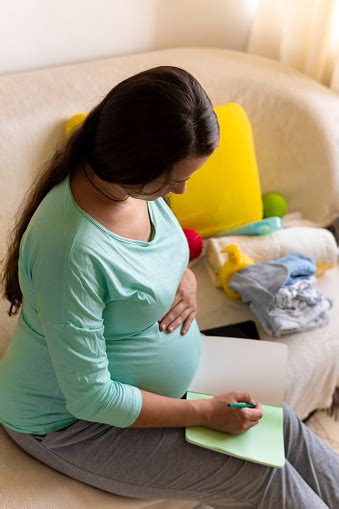 귀여운 임산부는 수첩이 있는 출산 병원에 포장 목록을 작성하여 가방을 준비합니다 임신 에 젊은 Ledy 는 집에서 소파에 즐거운 시간을 보내고있다 모성 의학 건강 및 관리