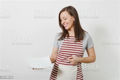 젊은 매력적인 웃는 갈색 머리 백인 주부 스트라이프 앞치마에 회색 티셔츠 흰색 배경에 고립 아름 다운가 정부 여자 흰색 빈 접시를 들고입니다 광고에 대 한 공간을 복사