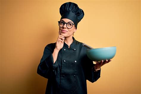 젊은 아름다운 갈색 머리 요리사 여자 밥솥 유니폼과 모자 를 들고 그릇을 입고 질문에 대해 생각 심각한 얼굴을 휘젓고 매우 혼란