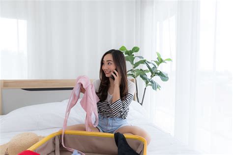 그녀의 드레스를 들고 노란색 수하물 여름 휴가 및 여행 준비 개념으로 물건을 준비하는 동안 휴대 전화를 사용하는 젊은 여성 20