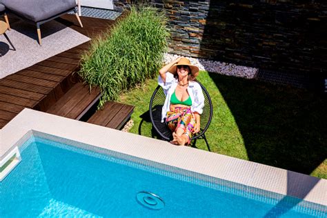 흰 셔츠와 밀짚모자를 쓰고 수영장 옆에서 휴식을 취하는 매력적인 여성 30 34세에 대한 스톡 사진 및 기타 이미지 30 34세 30 39세 가정 생활 Istock