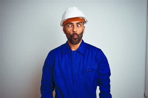 입술 미친 코믹 한 제스처와 물고기 얼굴을 만드는 고립 된 흰색 배경 위에 유니폼과 헬멧을 입고 잘 생긴 인도 노동자 남자 재미있는 표현 건설 산업에 대한 스톡 사진 및