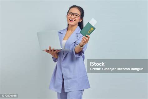 노트북을 사용하여 서 서 흰색 배경에 고립 된 쾌활한 표정으로 여권 책을 들고 서있는 젊은 아시아 여성의 초상화 여자 사업가에