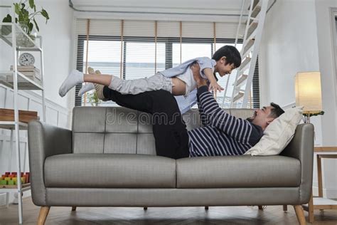 Asian Dad Plays With Son On A Sofa Lifting And Spreading Arms Like Plane Stock Photo Image Of