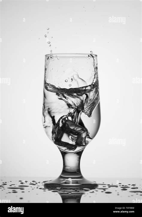 The Cube Of Ice Falls Into A Clear Glass Glass With Water Splash Of
