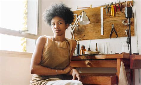 Portrait Of African Woman Sitting Next To Work Desk In Jewelry Workshop