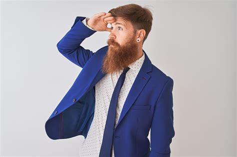 고립 된 흰색 배경 위에 서있는 양복을 입은 젊은 빨간 머리 아일랜드 사업가는 매우 행복하고 머리 위에 손으로 멀리 보고 미소 개념 검색 거리가 먼에 대한 스톡 사진 및