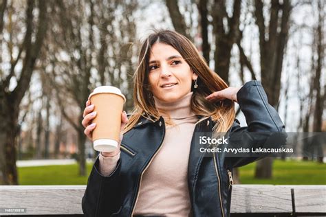 커피 종이컵을 들고 가을 공원의 벤치에서 휴식을 취하는 즐거운 젊은 여성 한 여자가 갈색 커피잔을 손에 들고 있다 가을 공원에 있는 여자 근접 촬영 30 34세에 대한 스톡