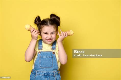 장난꾸러기 어린 소녀가 얼굴을 만들고 얼굴을 찡그리고 노란색 배경 위에 아이스크림 와플 콘을 들고 포즈를 취한다 고등학교 이하에 대한 스톡 사진 및 기타 이미지 Istock