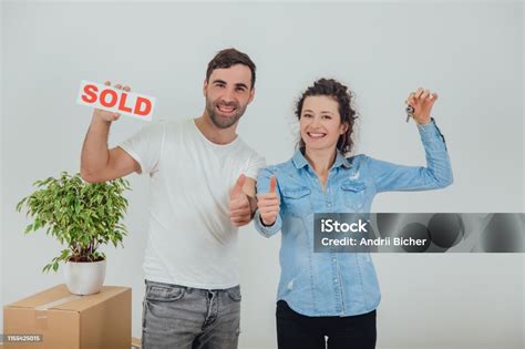 행복한 아내와 남편이 서서 엄지 손가락을 내치고 있습니다 여자는 자신의 아파트에 열쇠를 들고있다 남자가 카메라를 바라보며 빨간 단어가 적힌 접시를 들고 있다 집에 대한 스톡