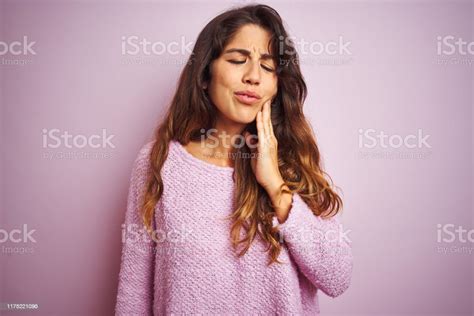 분홍색 고립 된 배경 위에 서있는 스웨터를 입은 젊은 아름다운 여성은 치아에 치통이나 치과 질환으로 인해 고통스러운 표정으로