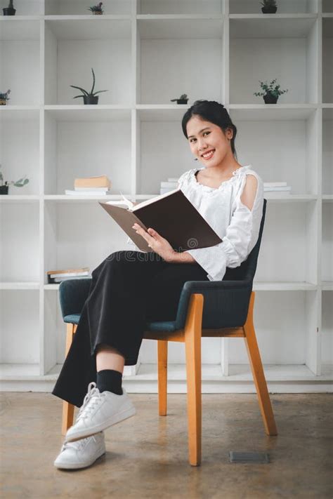 Side View Of Asian Woman Sitting Armchair With Open Book And Reading