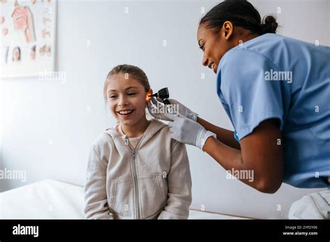 Happy Female Medical Expert Examining Ear Of Girl With Flashlight In