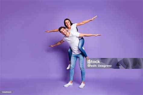 전체 길이 바디 사이즈 사진 의 쾌활 한 흥분 긍정적인 커플 그녀의 승마 그의 뒤로 팔 과 측면 에 흰색 신발 티셔츠 청바지