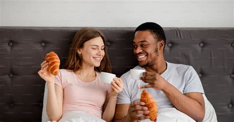 밀레니얼 세대의 다인종 커플은 침대에서 함께 아침을 먹고 크루아상과 함께 커피를 마시고 호텔에서 신혼여행을 보낸다 맛있는 식사와 함께 낭만적인 아침을 즐기는 다민족