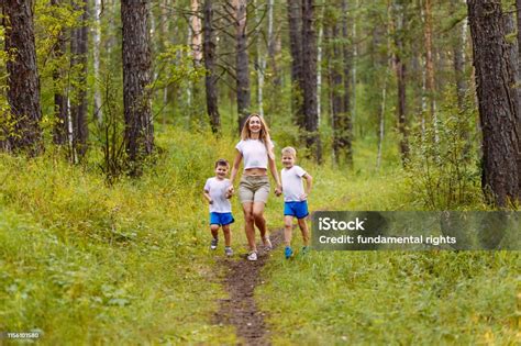 젊은 날씬한 아름다운 여자와 흰색 티셔츠를 입은 두 명의 미취학 아동이 여름에 손을 잡고 길을 따라 달려간다 T 셔츠에 대한