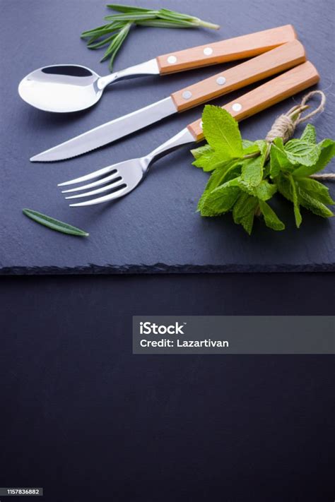 칼 세트입니다 칼 숟가락 슬레이트 돌에 포크 로즈마리와 민트가 있는 크립토클러 검은 색 배경입니다 공간을 복사합니다 맨 위 보기 0명에 대한 스톡 사진 및 기타 이미지