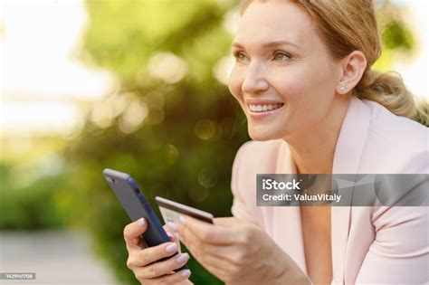 신용 카드와 전화를 가진 사업가가 야외에서 구매합니다 성공적인 여성은 온라인 쇼핑을 위해 스마트 폰과 은행 카드를 사용하고 있습니다 아름다운 미소 짓는 백인 여성이 카드와