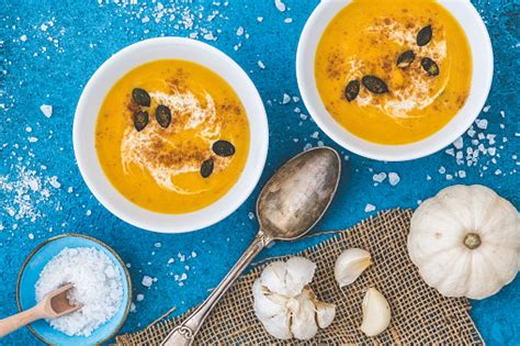 호박 당근 수프는 파란색 배경에 크림과 호박 씨앗과 두 개의 흰색 그릇에 제공됩니다 수직 상단 보기입니다 가을에 대한 스톡 사진 및 기타 이미지 Istock