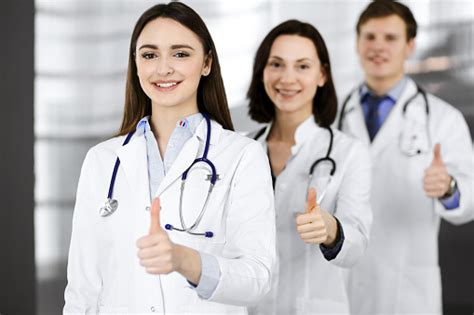 젊은 쾌활한 의사 그룹이 병원 사무실에서 엄지 손가락을 치켜 들고 팀으로 서서 환자를 도울 준비가되어 있습니다 의료 지원 건강 관리 보험 최고의 질병 치료 및 의학 개념