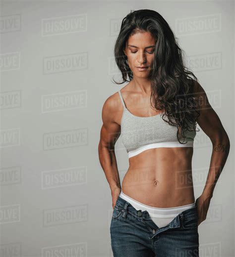 Fit Young Woman Pulling Down Pants With Copy Space To Her Side Over Gray Background Stock