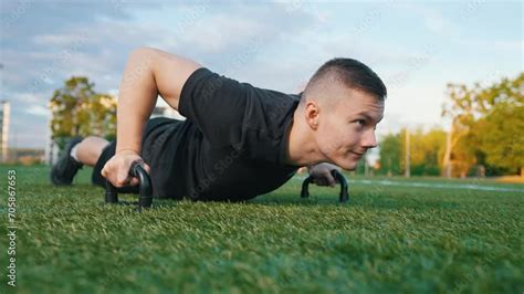Guy Exercising Outdoors He Does Push Ups On The Push Up Platform At Stadium Green Grass Field