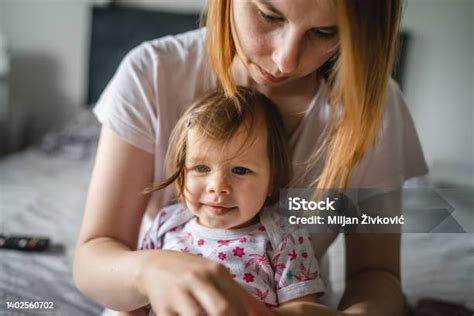 그녀의 어머니가 옷을 갈아 입고있는 동안 집에서 침대에 앉아있는 한 작은 백인 소녀 유아는 복사 공간을 자라는 실제 사람들 12 17 개월에 대한 스톡 사진 및 기타 이미지