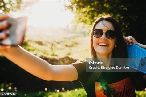 Selfie 일몰에 대 한 웃음을 하 고 선글라스와 함께 그녀의 어깨에 스케이트 보드와 함께 사랑 스러운 젊은 백인 여자 거리에 대한 스톡 사진 및 기타 이미지 Istock