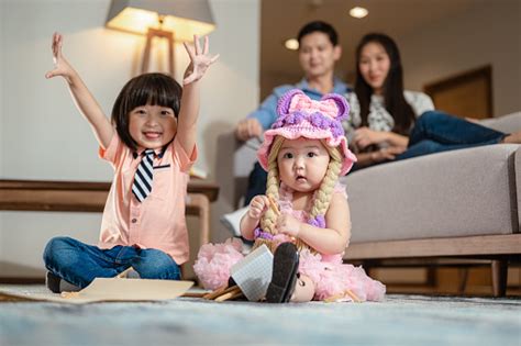 동생은 여동생과 놀고 있었습니다 그는 손을 들어 집 거실에 있는 양탄자에 있는 여동생을 바라보며 웃었고 부모님은 소파에 앉아 멀리 서 있는 것을 보았습니다 가정 개념의 가족