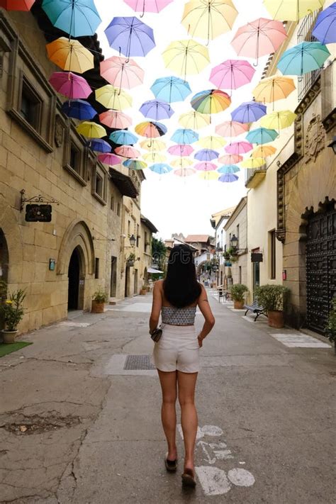 Vertical Back View Of A Female In Short Walking In An Alley With Overhead Hanging Colorful