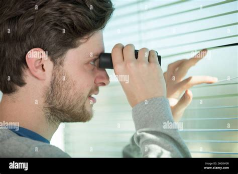 Young Man Standing Looking Through A Glass Window With Binoculars Stock