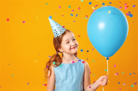 파티에서 쾌활 한 어린 소녀입니다 아이는 색종이의 비에 파란 공을 보유 하 고 있습니다 노란색 배경에 근접 촬영 초상화입니다 색종이 조각에 대한 스톡 사진 및 기타 이미지