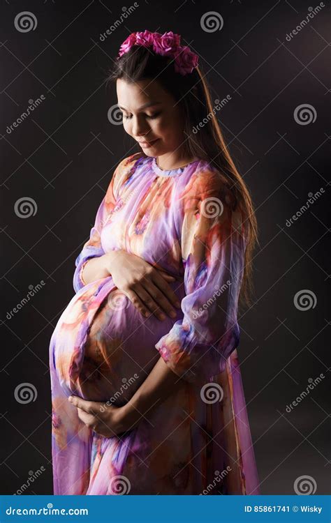 Беременная женщина с руками на животе представляя на темноте Стоковое Изображение изображение