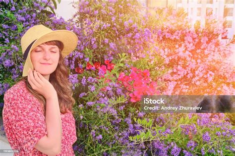 빨강 파랑 분홍색 꽃의 배경에 모자를 쓴 소녀 복사 공간 빨간 드레스를 입은 한 여성이 미소를 지으며 밀짚 모자를 손에 들고 있다 꽃 나무에 대한 스톡 사진 및 기타 이미지