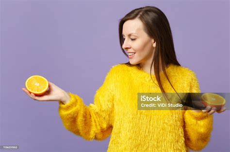 스튜디오에서 보라색 파스텔 배경에 고립 된 신선한 잘 익은 오렌지 과일의 Halfs를 찾고 들고 모피 스웨터에 예쁜 젊은 여자 사람들은 생생한 라이프 스타일 휴식 휴가