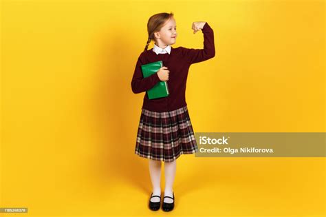 노란색 배경에 유니폼을 입은 전체 길이 여학생 어린 소녀는 손의 힘을 보여주고 책을 들고 전신에 대한 스톡 사진 및 기타 이미지