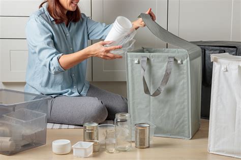 아시아계 혼혈인 젊은 여성이 부엌 바닥에 앉아 재활용품을 별도의 봉투에 꼼꼼하게 분류하고 있습니다 그녀는 플라스틱 재료를 분리하여 적절한 재활용 수거를 준비합니다 0에 대한