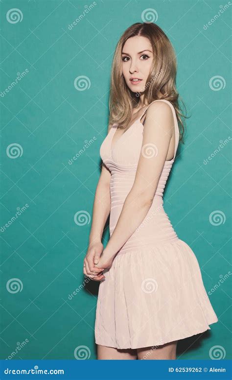 Устрашенная девушка стоя в коротком розовом платье представляя на зеленой предпосылке в студии