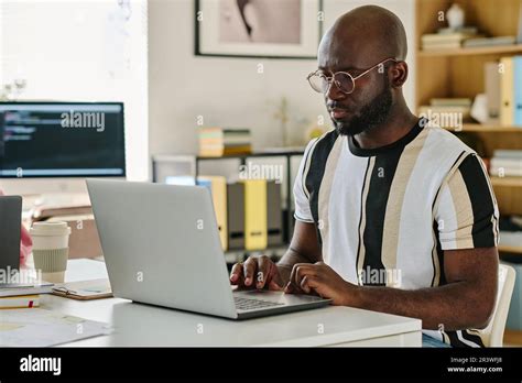Serious African American Programmer Typing Codes On Laptop Sitting At His Workplace In It Office